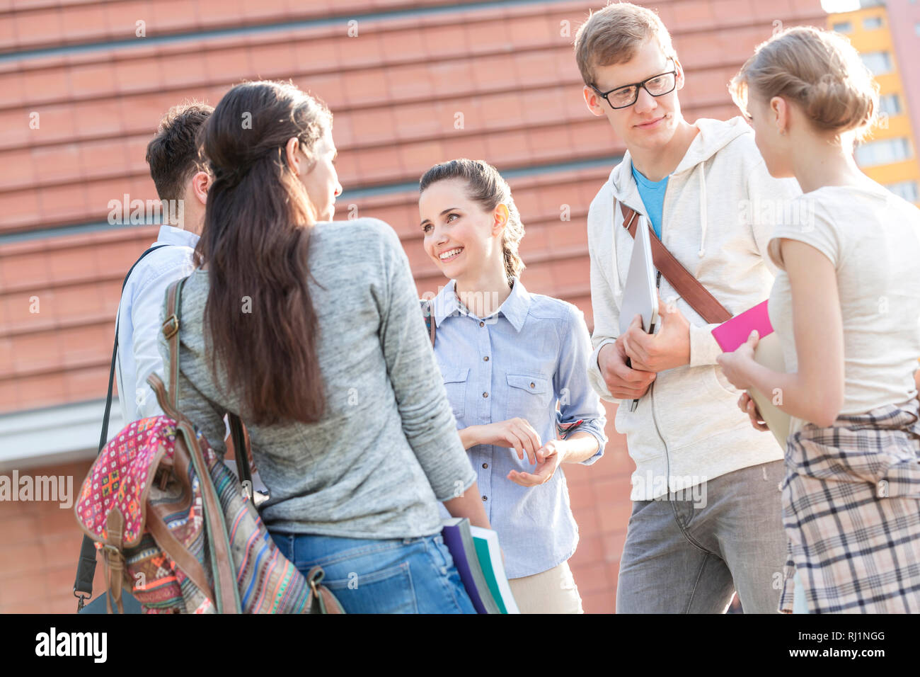 Happy students talking while standing in university campus Stock Photo ...