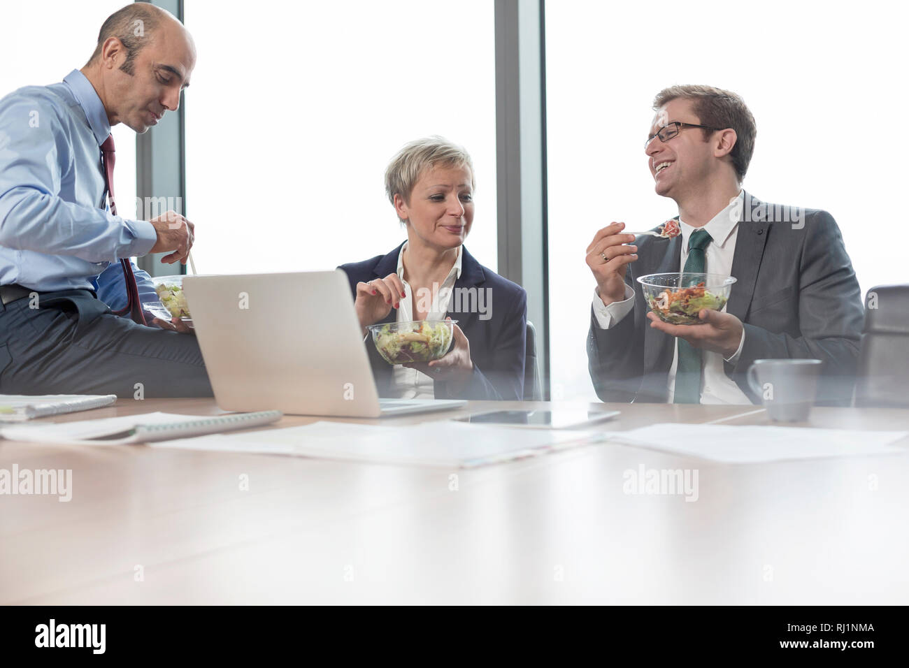 Smiling business colleagues eating lunch while sitting in boardroom ...