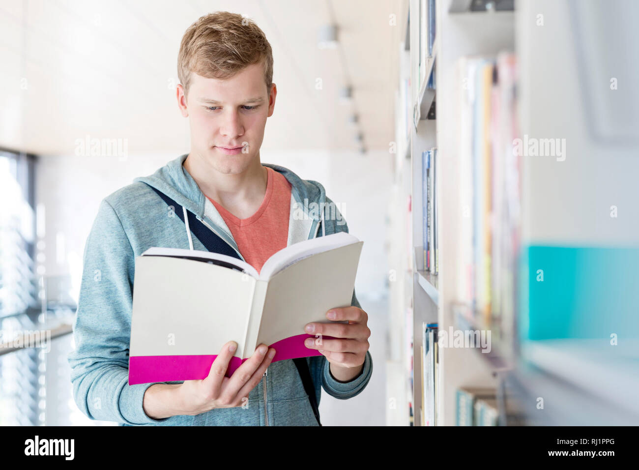 Serious young man reading book at university library Stock Photo - Alamy