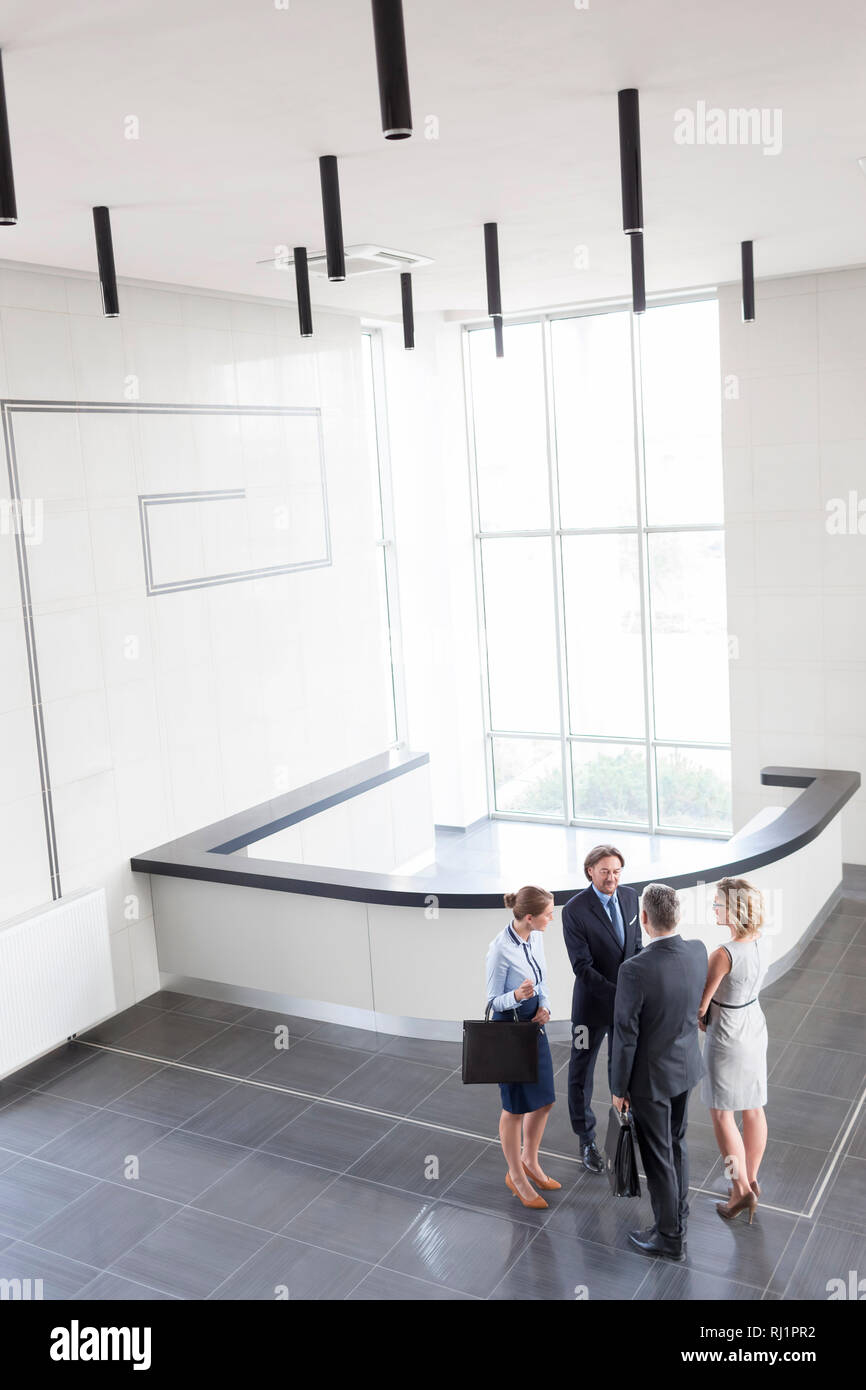 Businessmen greeting while standing with colleagues at reception lobby ...