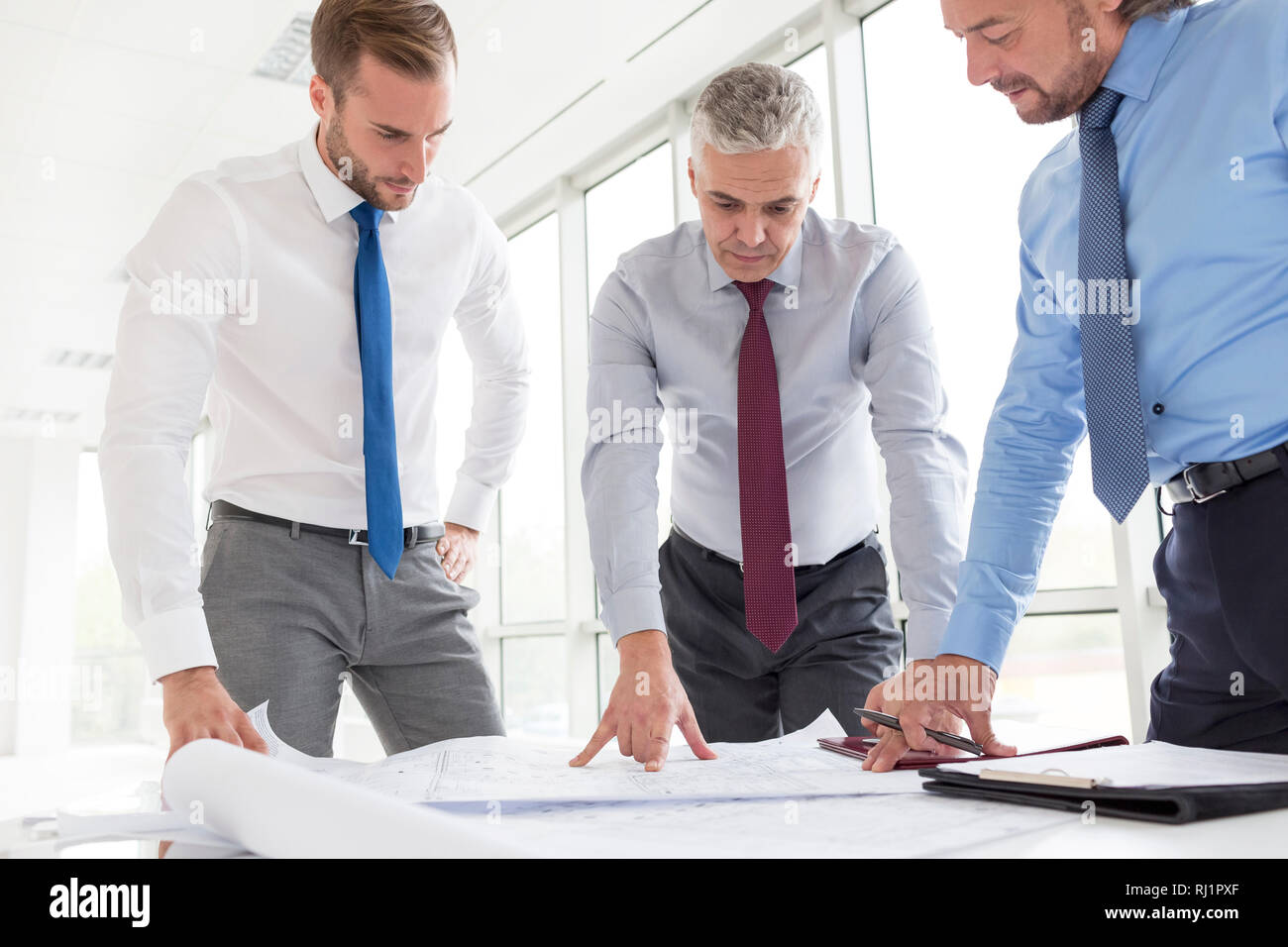 Businessmen analyzing blueprints at table in new office Stock Photo - Alamy