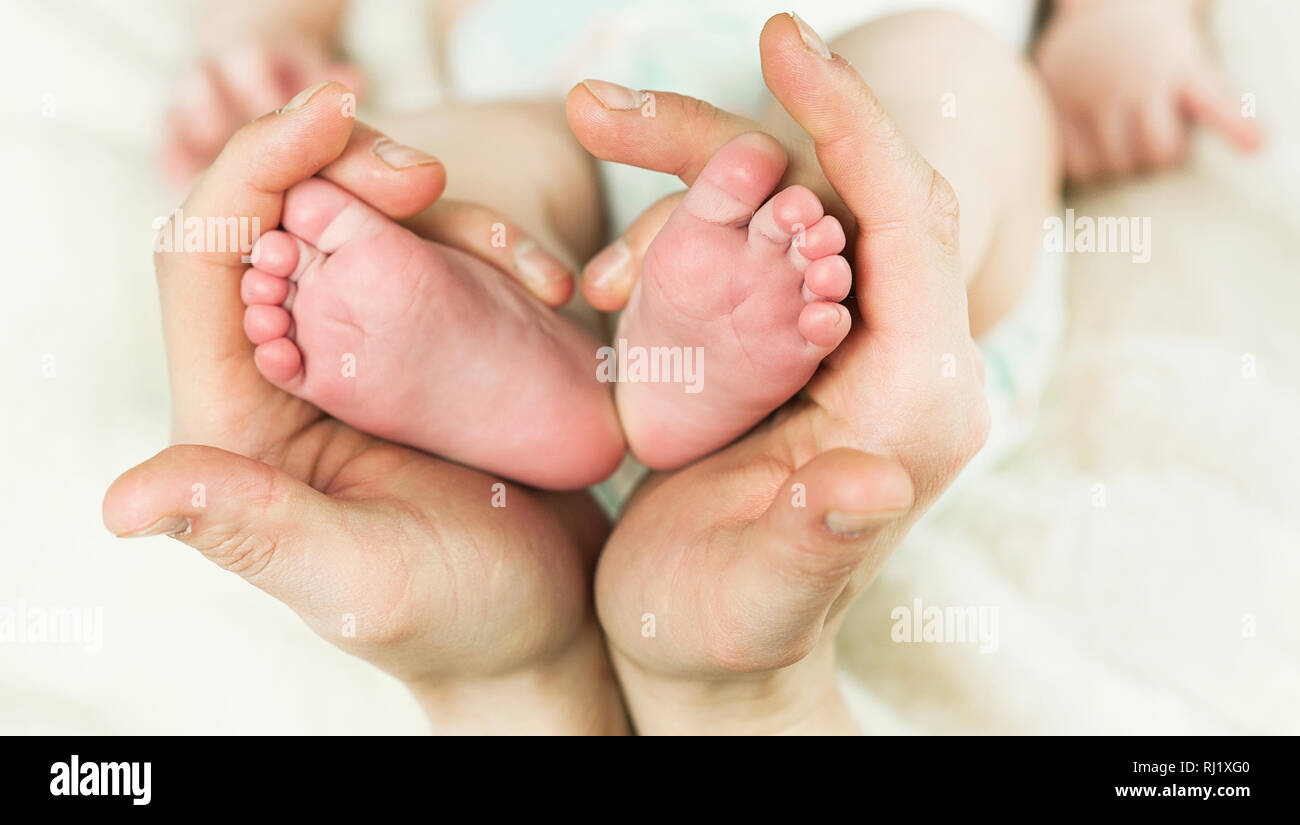 Close-up mother hand holding newborn baby feet in hear shape. Macro ...
