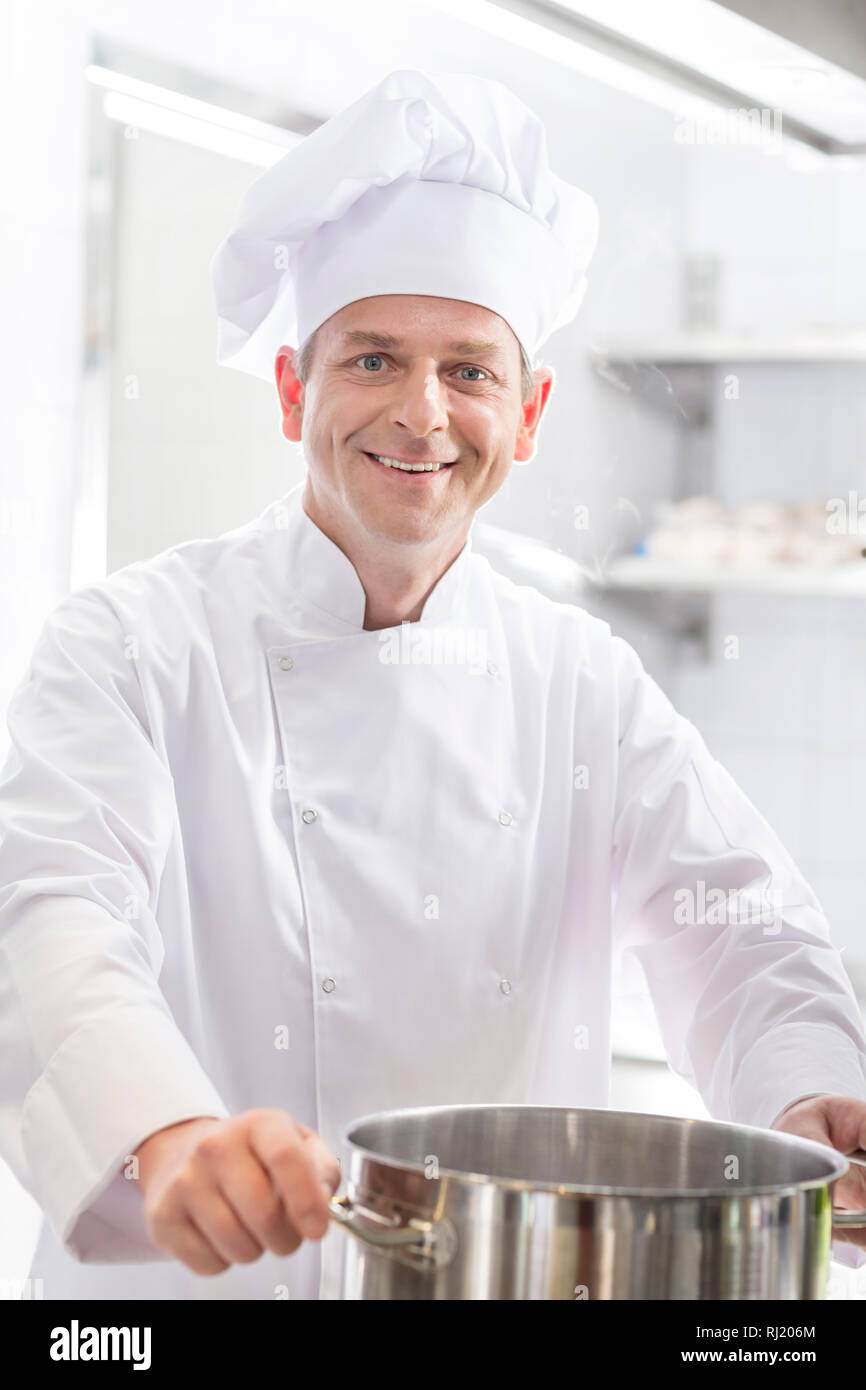 Portrait of smiling mature chef with steel cooking pot in kitchen at ...