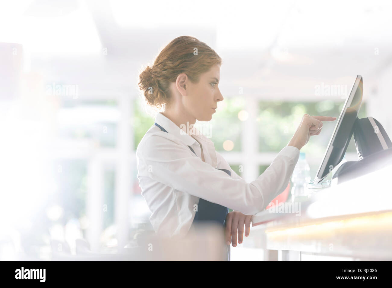 Side view of confident young waitress using computer while standing at ...