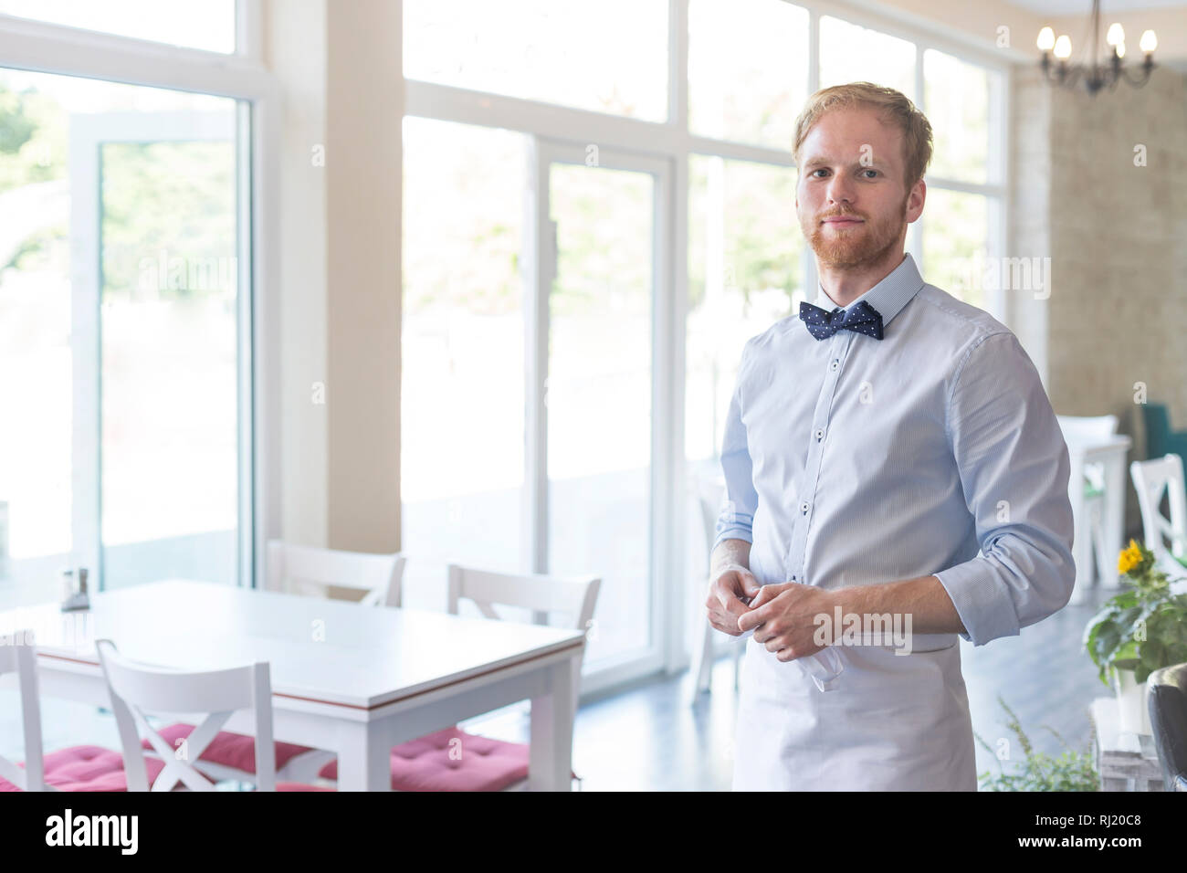 Portrait of confident young waiter standing at restaurant Stock Photo ...