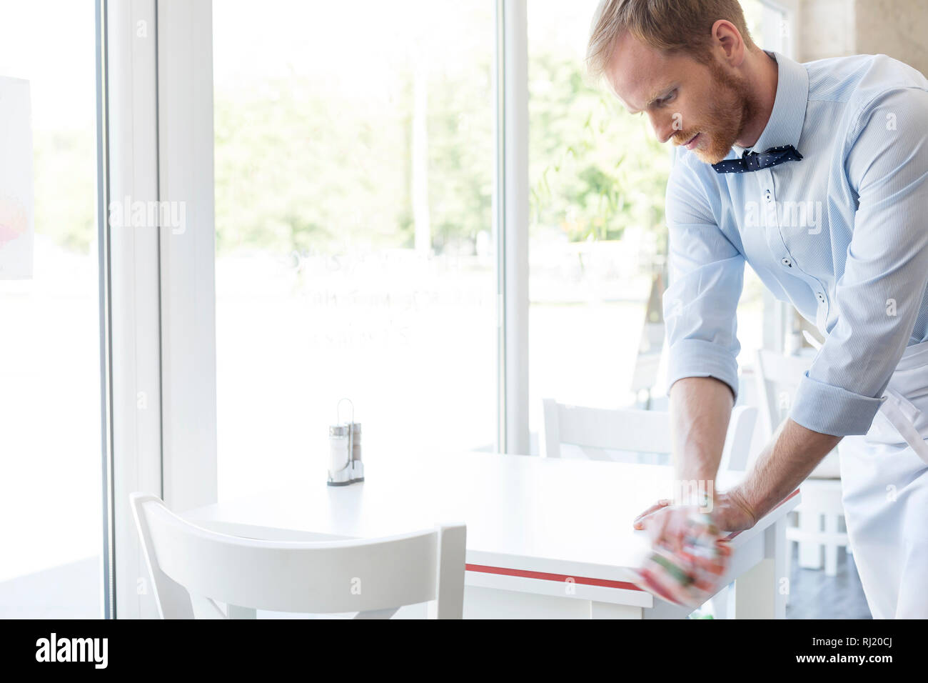 Confident young waiter cleaning table at restaurant Stock Photo - Alamy