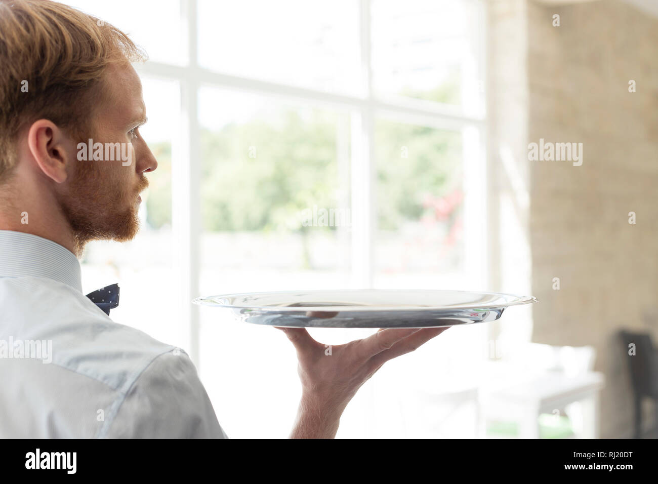 Rear view of confident young waiter holding tray while standing at ...