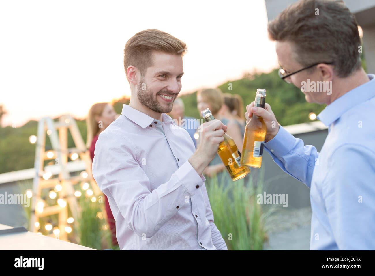 Businessmen toasting beer bottles during success party on rooftop Stock ...