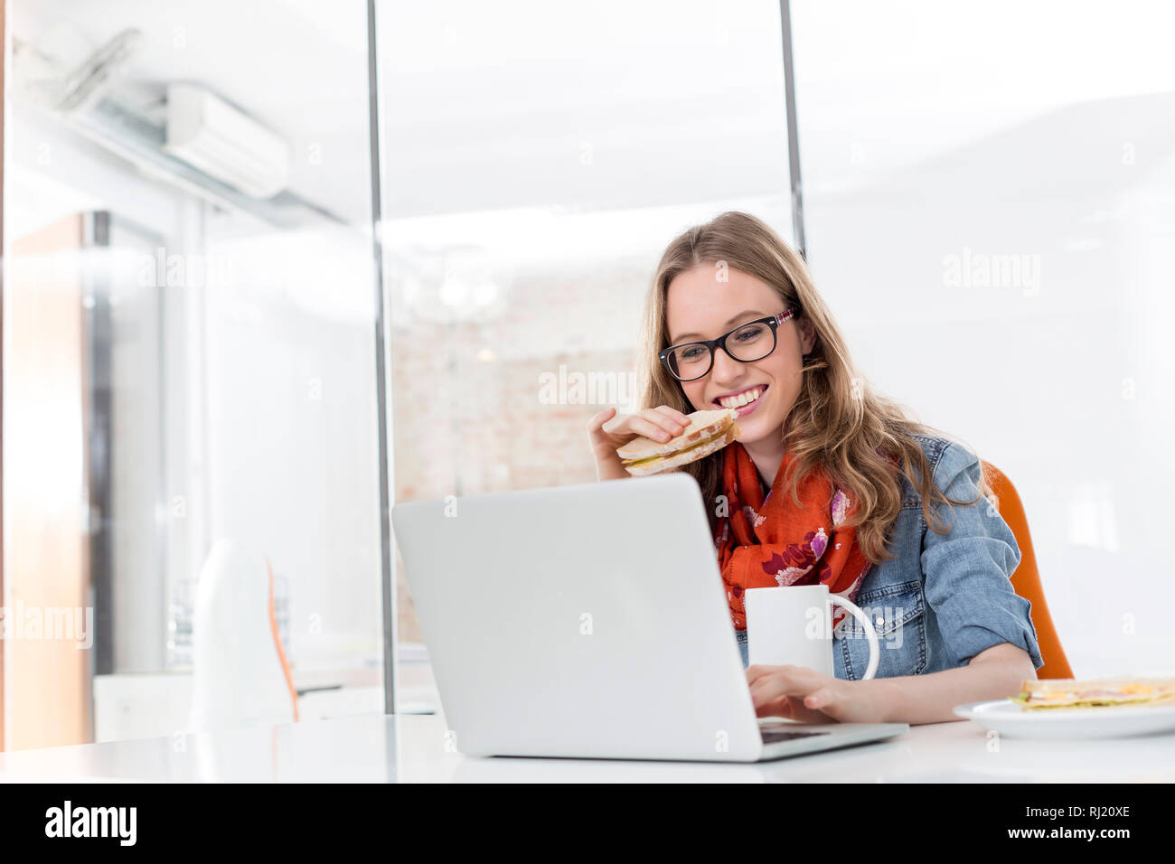 Creative businesswoman having breakfast while working on laptop in ...
