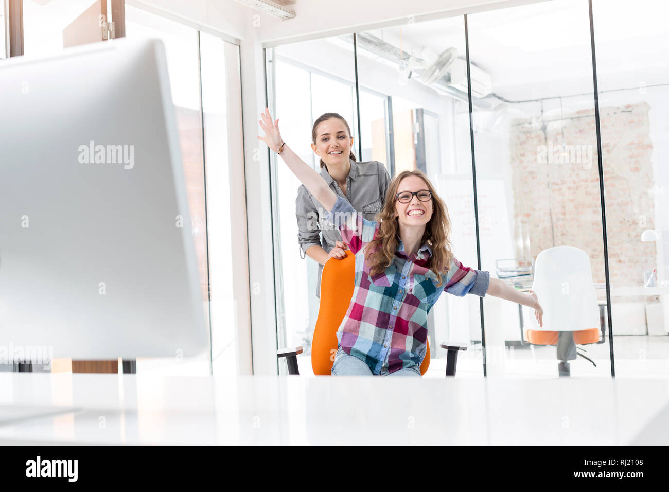 Businesswoman pushing playful colleague in office chair Stock Photo - Alamy