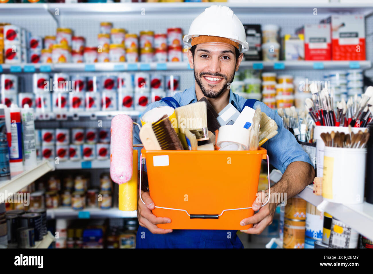 Positive smiling workman holding basket with picked tools in paint ...