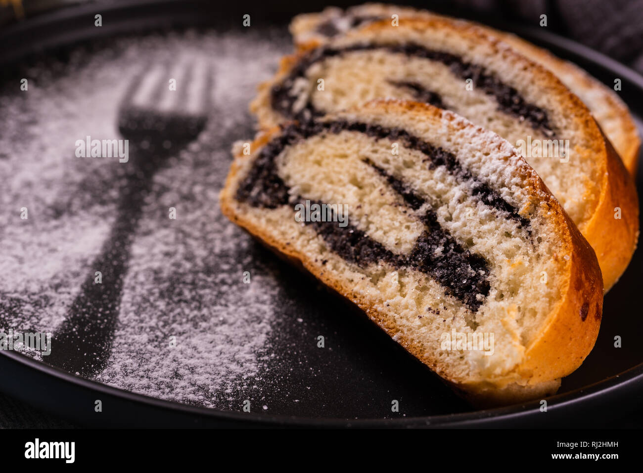 Poppy seed strudel on dark plate with silhouette of fork made by sugar ...
