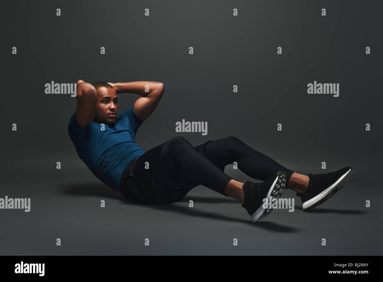 Dark skinned man in sportswear is concentrated while working abs, lying ...