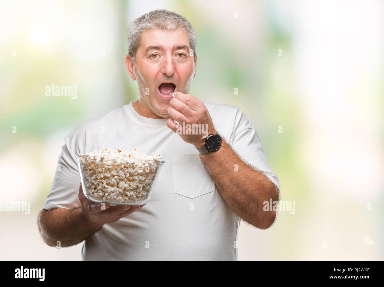 Handsome senior man eating popcorn over isolated background with a ...