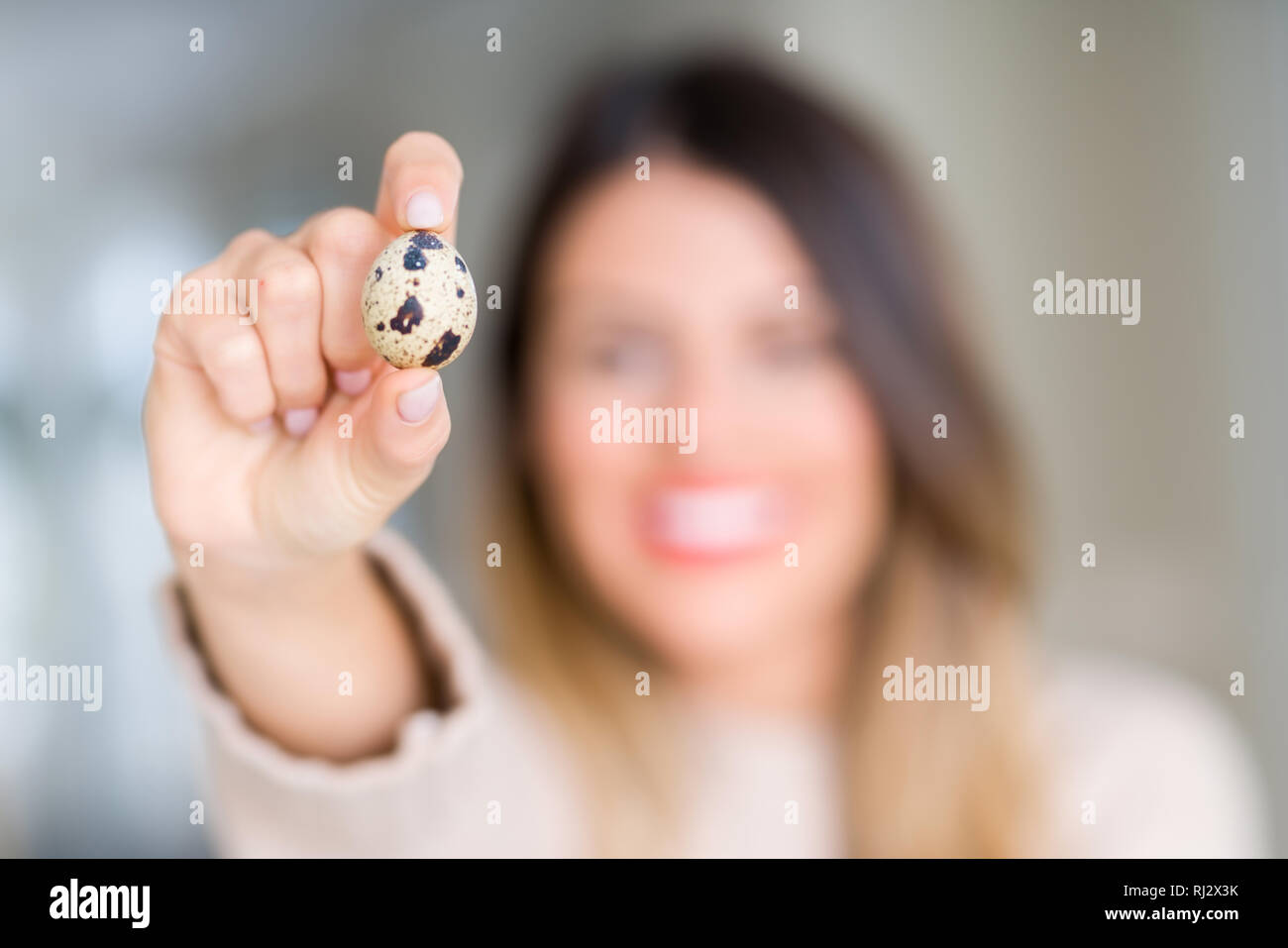Young beautiful woman holding fresh quail egg at home with a happy face ...