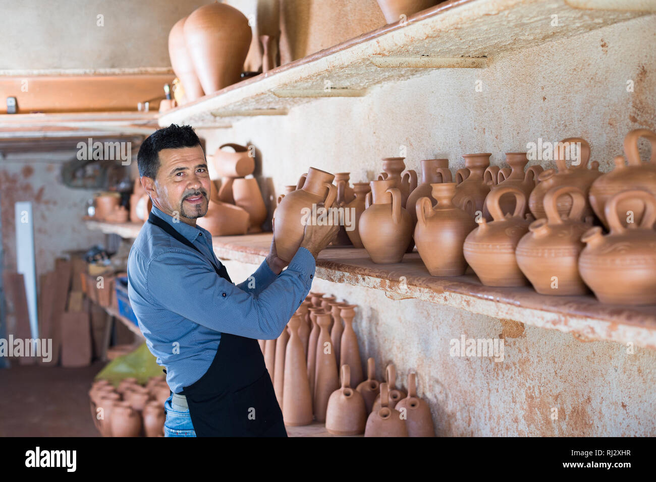 Smiling male sculptor having ceramics in hands and standing in pottery ...