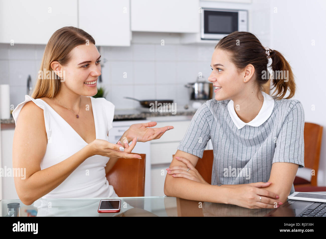 Portrait of two girls friends having expressional talking in kitchen ...