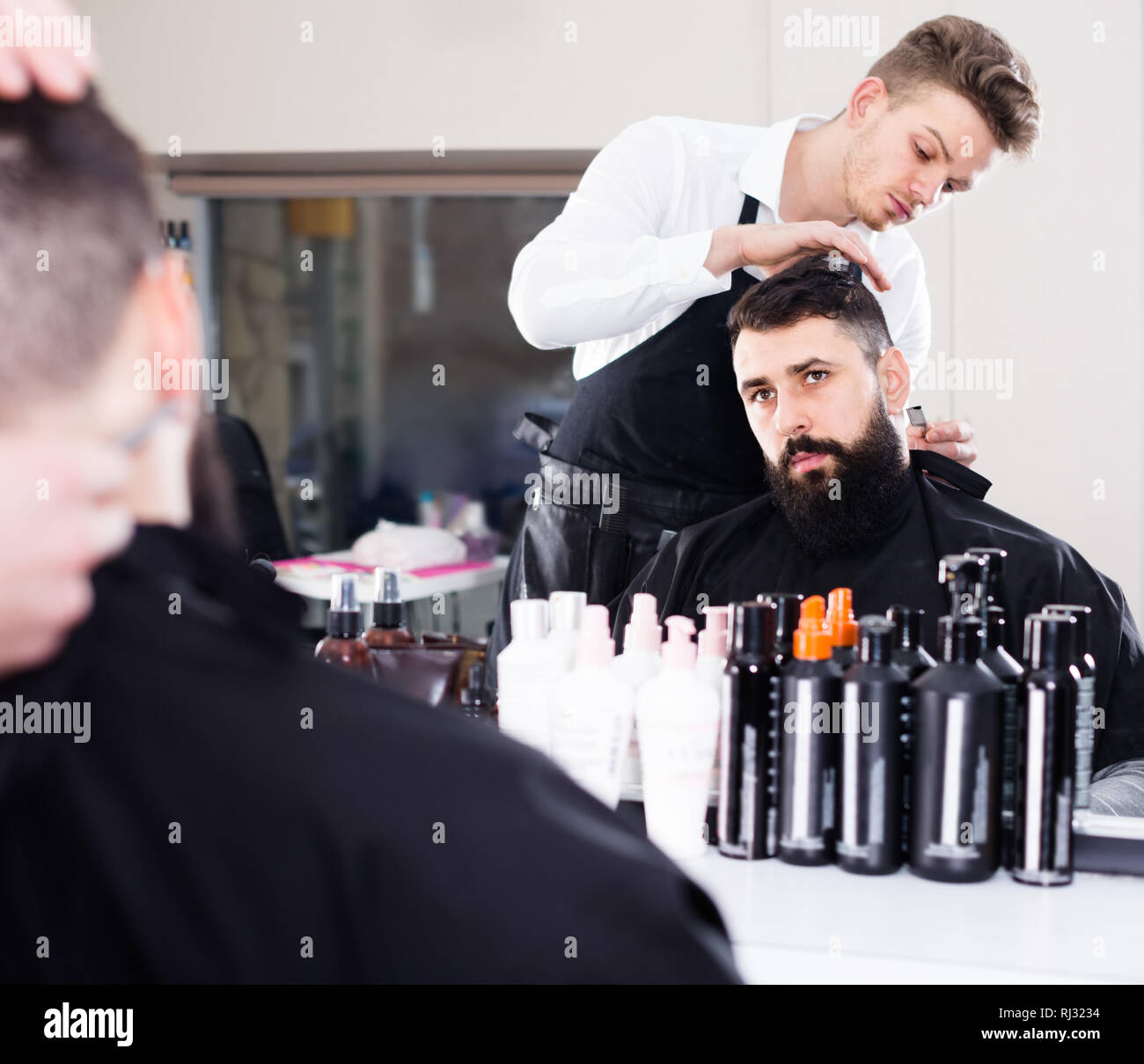 concentrated male stylist creating new haircut for man client at ...