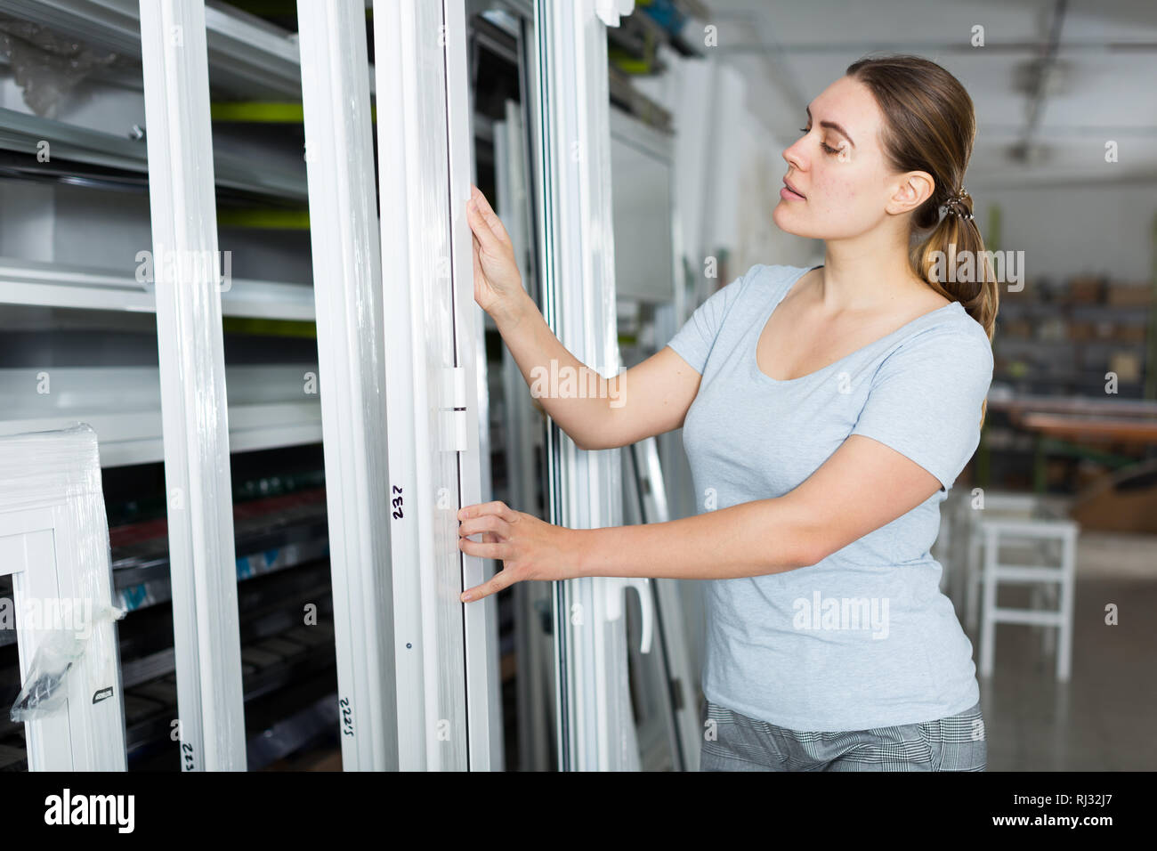 Portrait of woman who is looking on modern windows in the pvc workshop ...