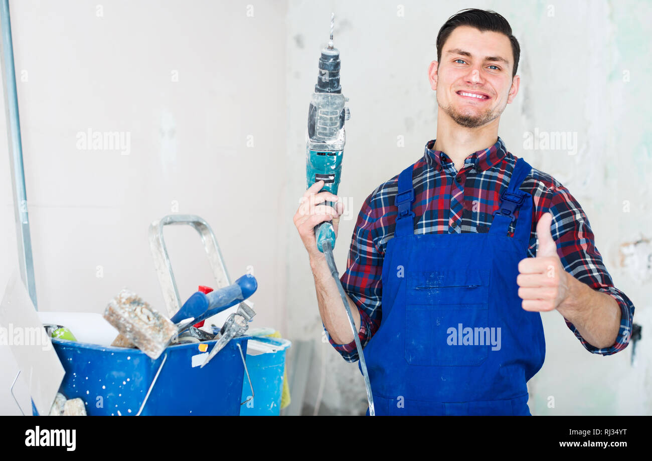 Young happy builder handyman with hammer in hand giving thumbs up in ...