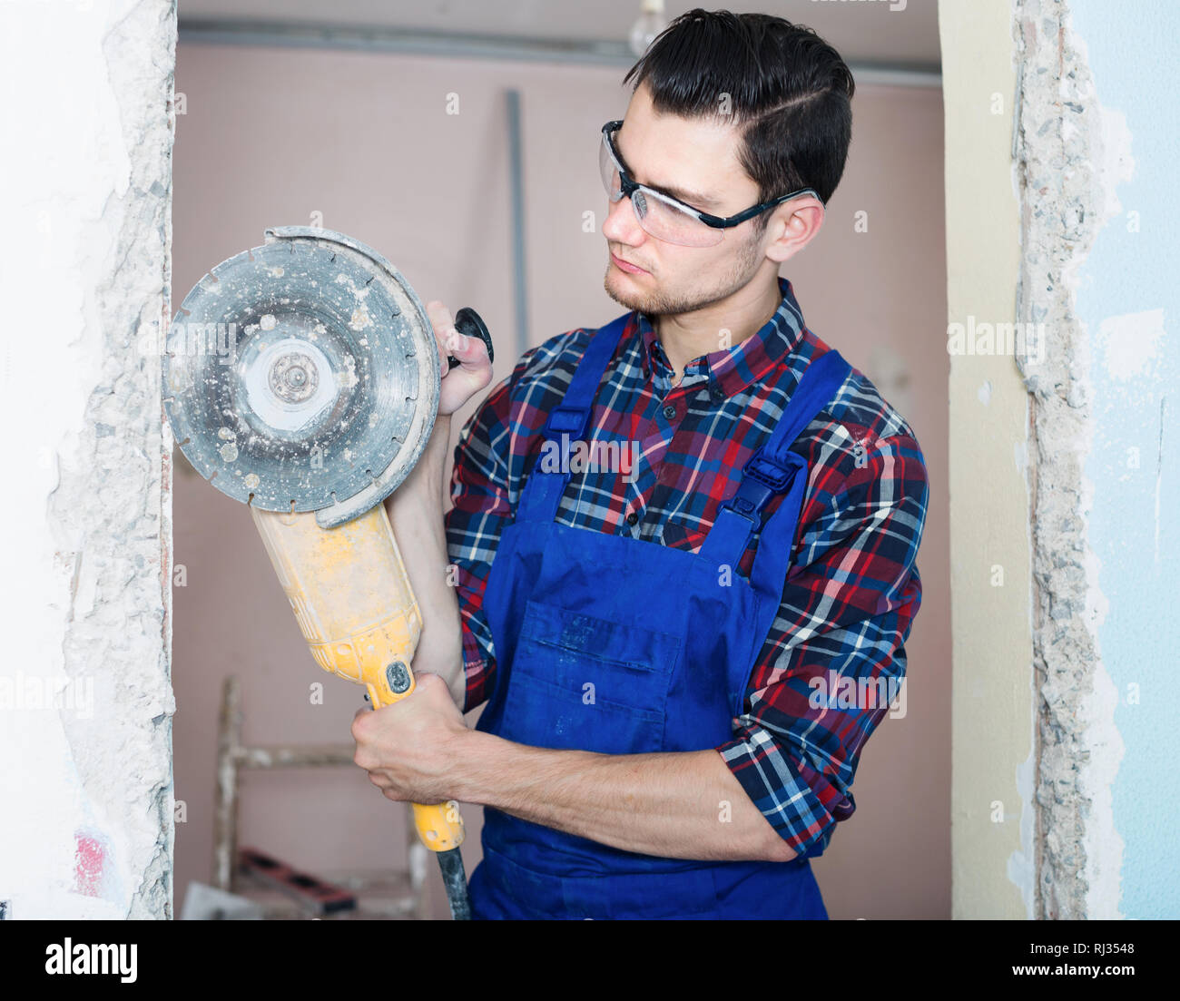 Young man worker using professional angle grinder for cutting wall ...