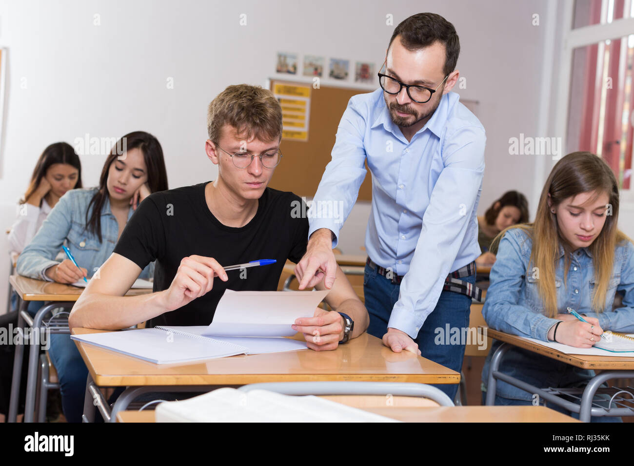 Schoolboy is writing answer the question on paper and teacher ...