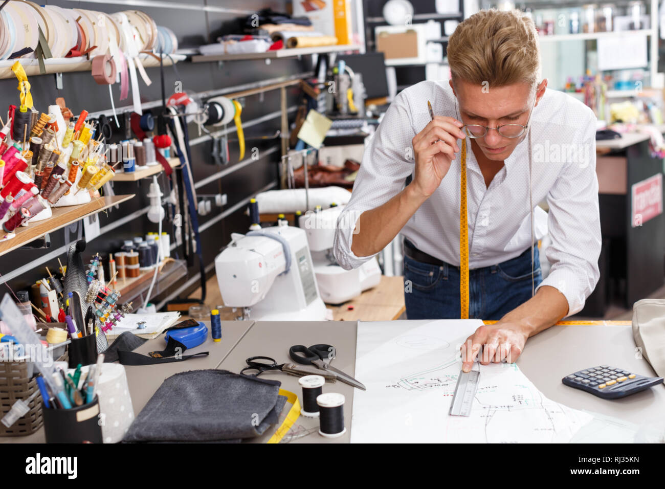 Confident male tailor using tape measure for creating pattern at sewing ...