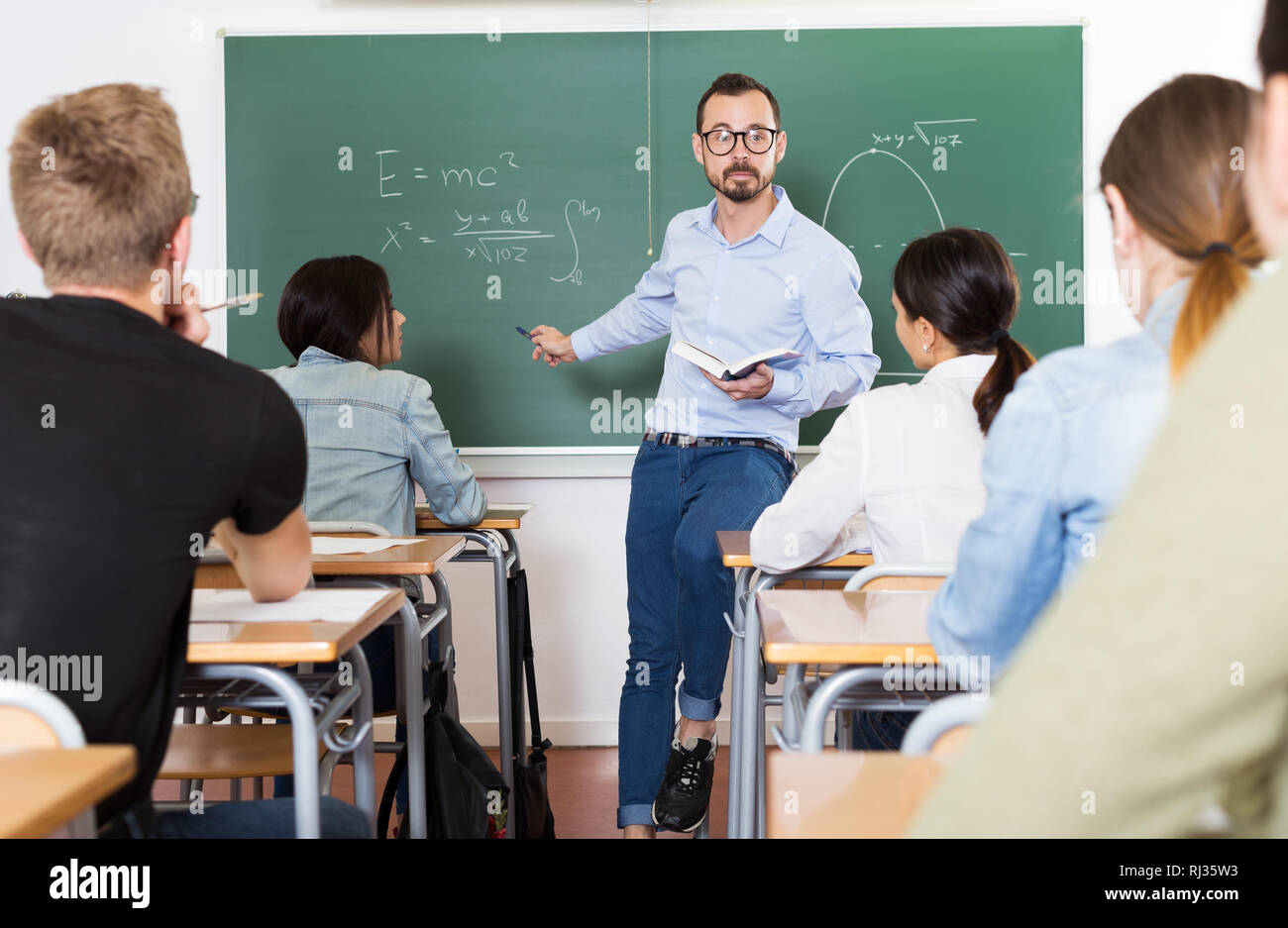 adult teacher is giving lecture for students with book in the class ...