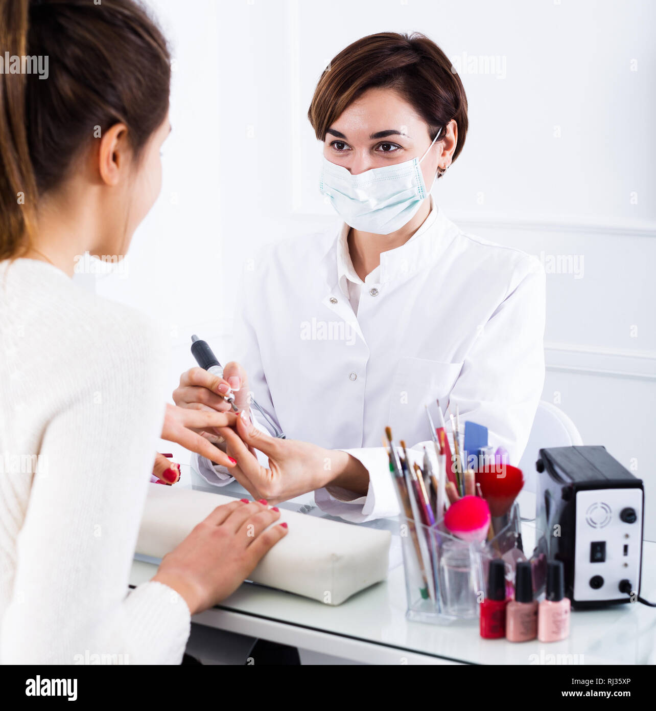 Positive adult woman doing manicure in shellac technique in nail salon ...