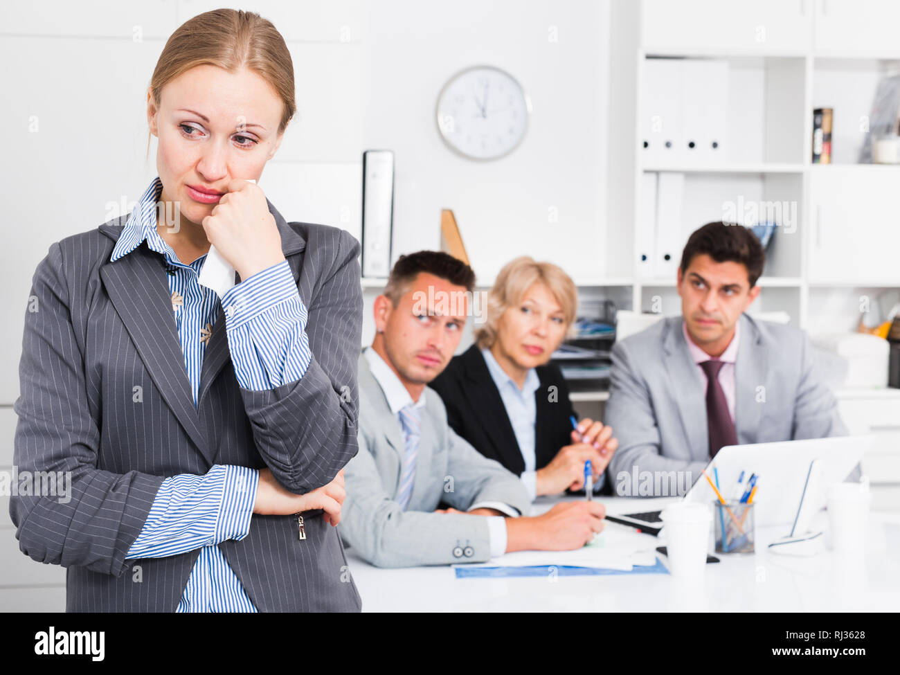 Business woman crying standing in office with working colleagues behind ...