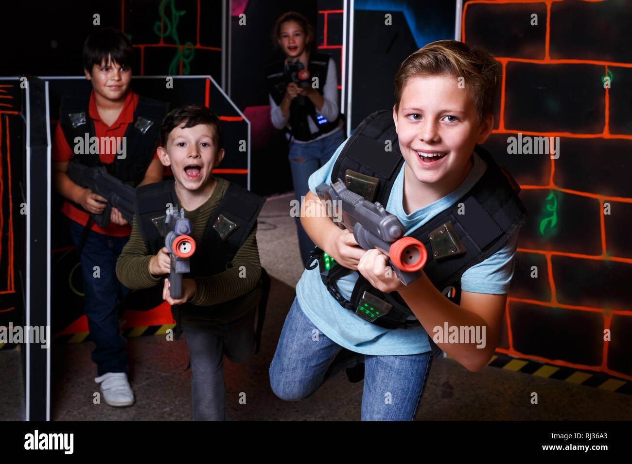 portrait of excited active young boy aiming laser gun at other players ...