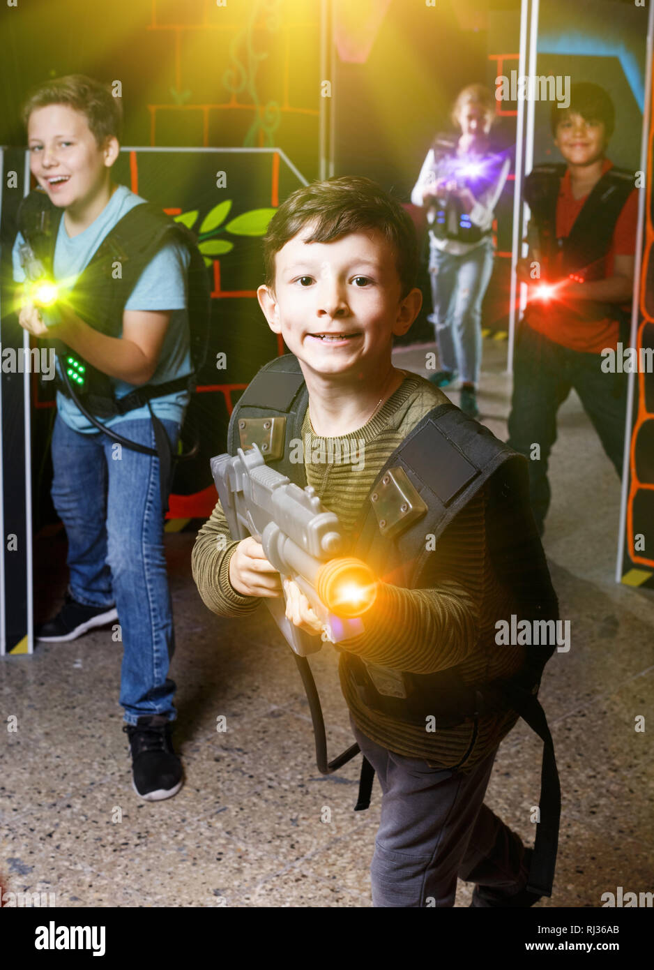 smiling active young boy aiming laser gun at other players during ...