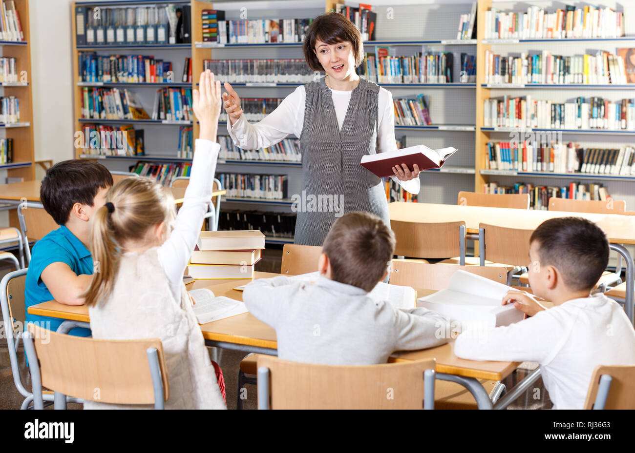 Portrait of young female librarian and diligent schoolkids during ...