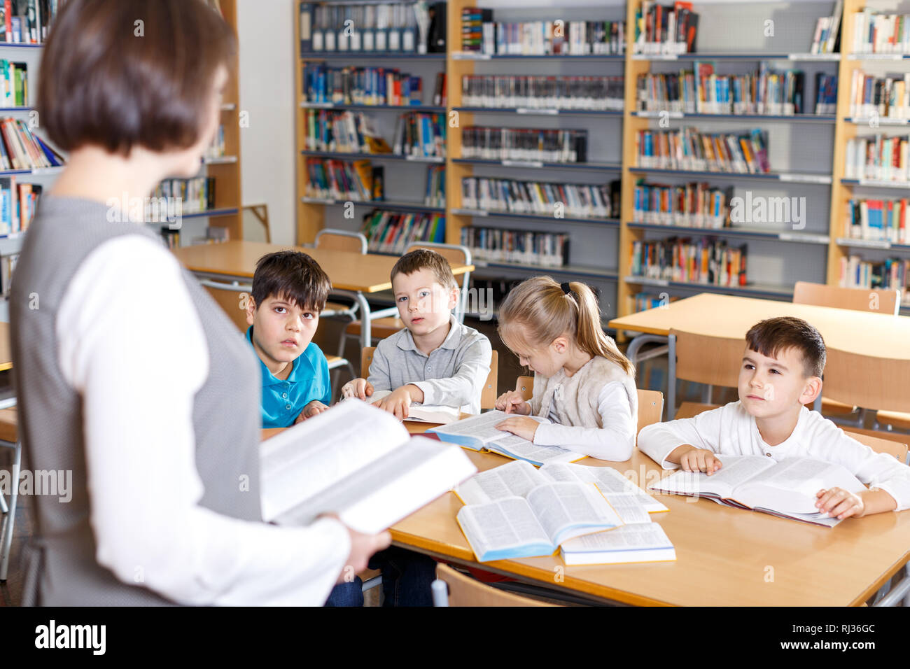 Portrait of young female librarian and diligent schoolkids during ...