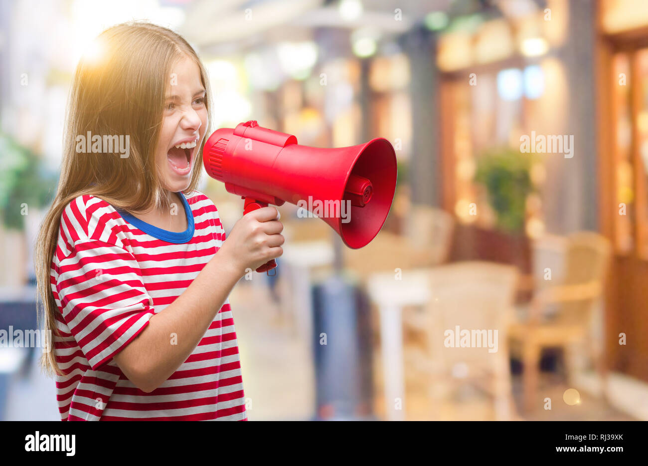 Young beautiful girl yelling through megaphone over isolated background ...