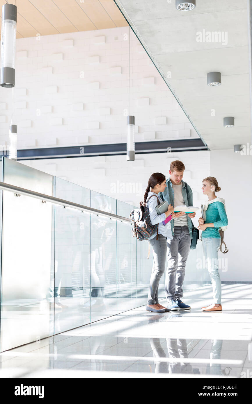 Students discussing over book in corridor at university Stock Photo - Alamy