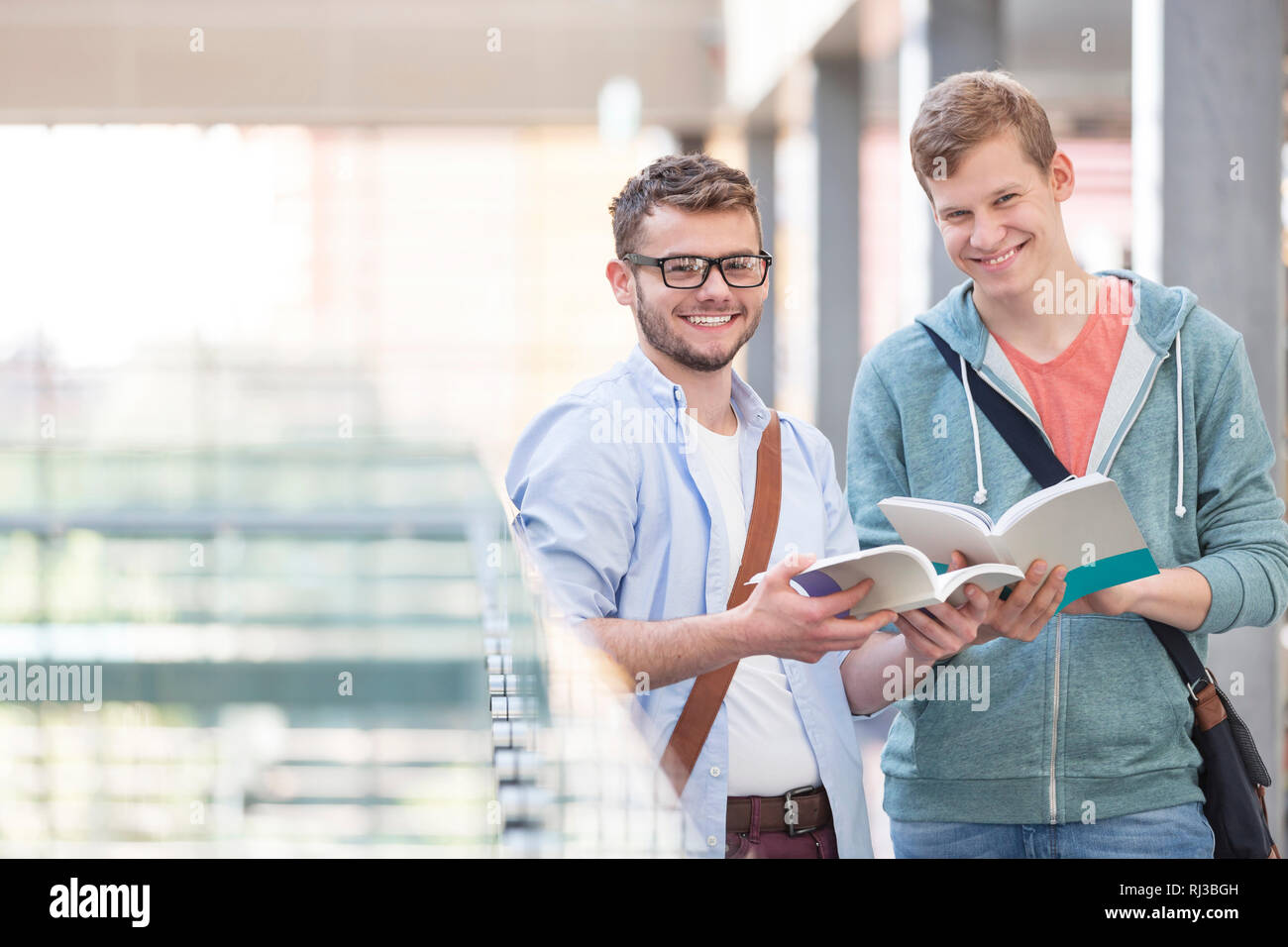Portrait of smiling friends with books standing at university corridor ...