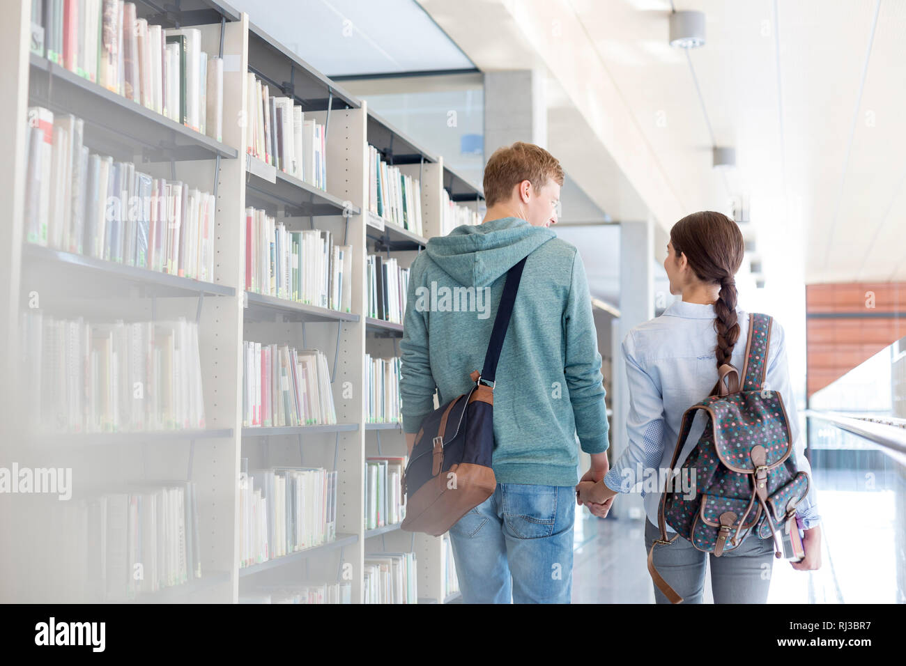 Rear view of couple walking while holding hands in library Stock Photo ...