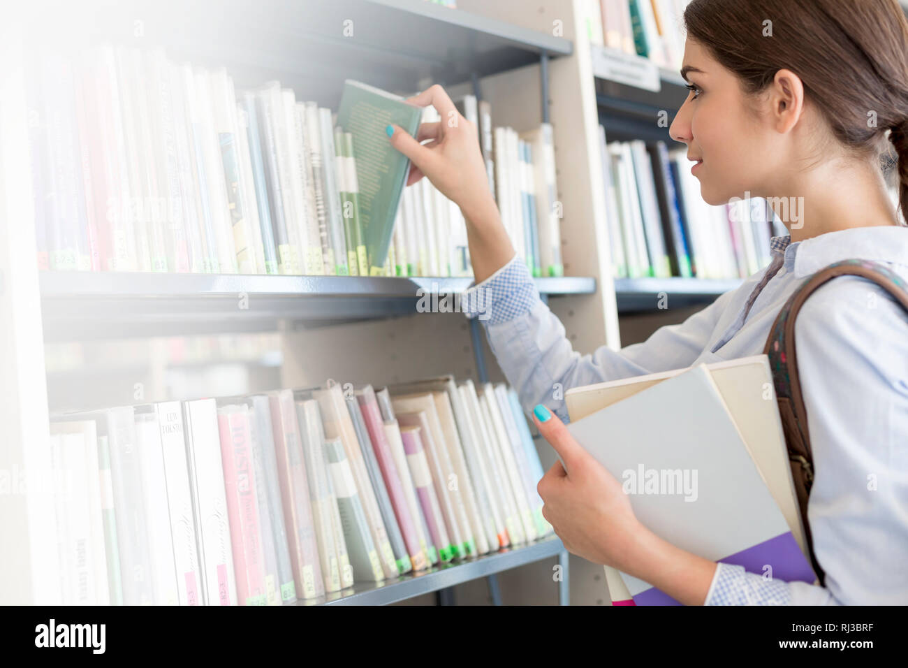 Teenage girl searching for book on shelf at library Stock Photo - Alamy