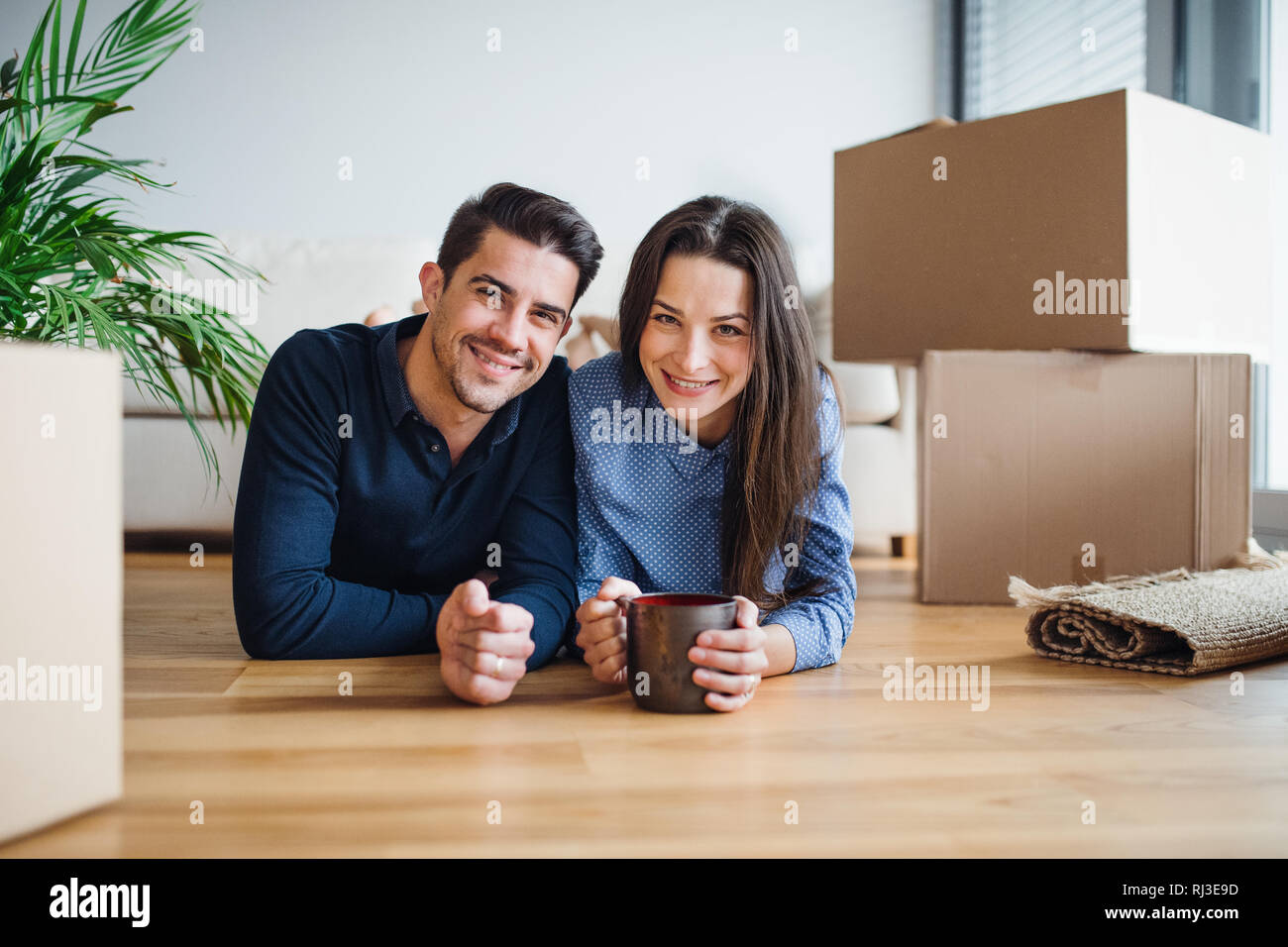 A young couple with a cup and cardboard boxes moving in a new home ...