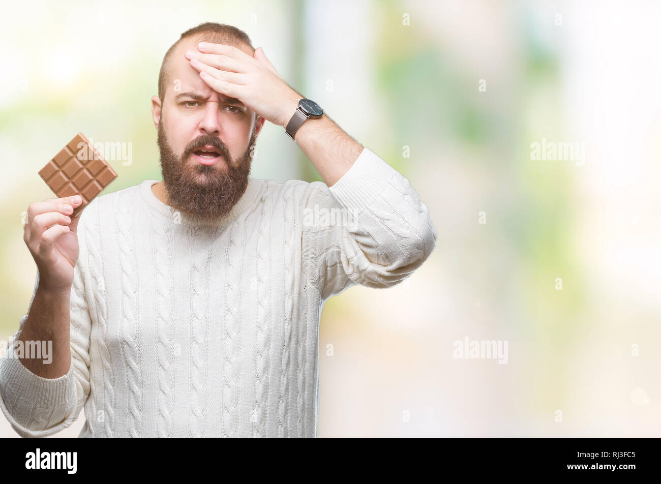 Young hipster man eating chocolate bar over isolated background ...