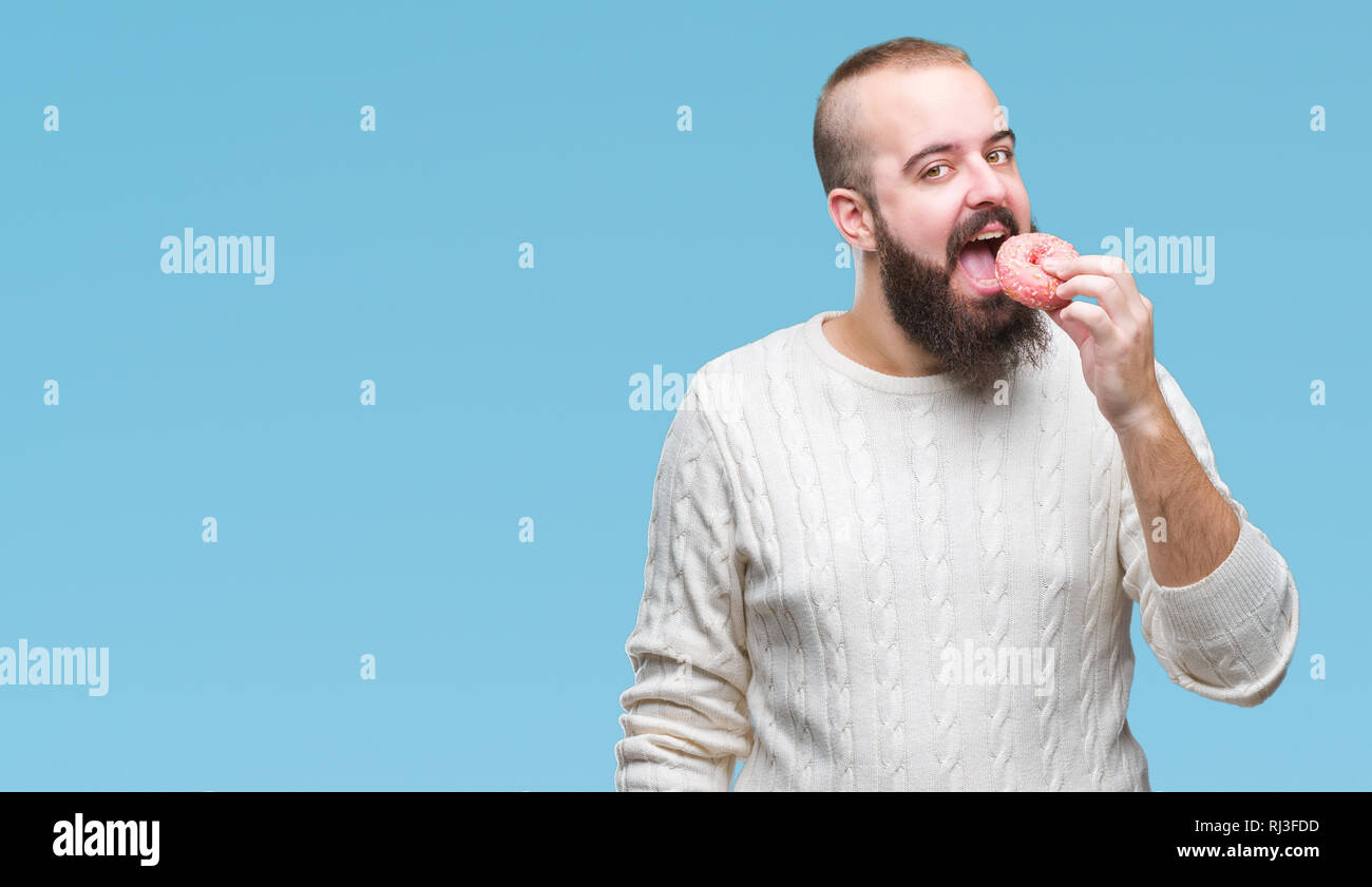 Young caucasian hipster man eating sweet donut over isolated background ...