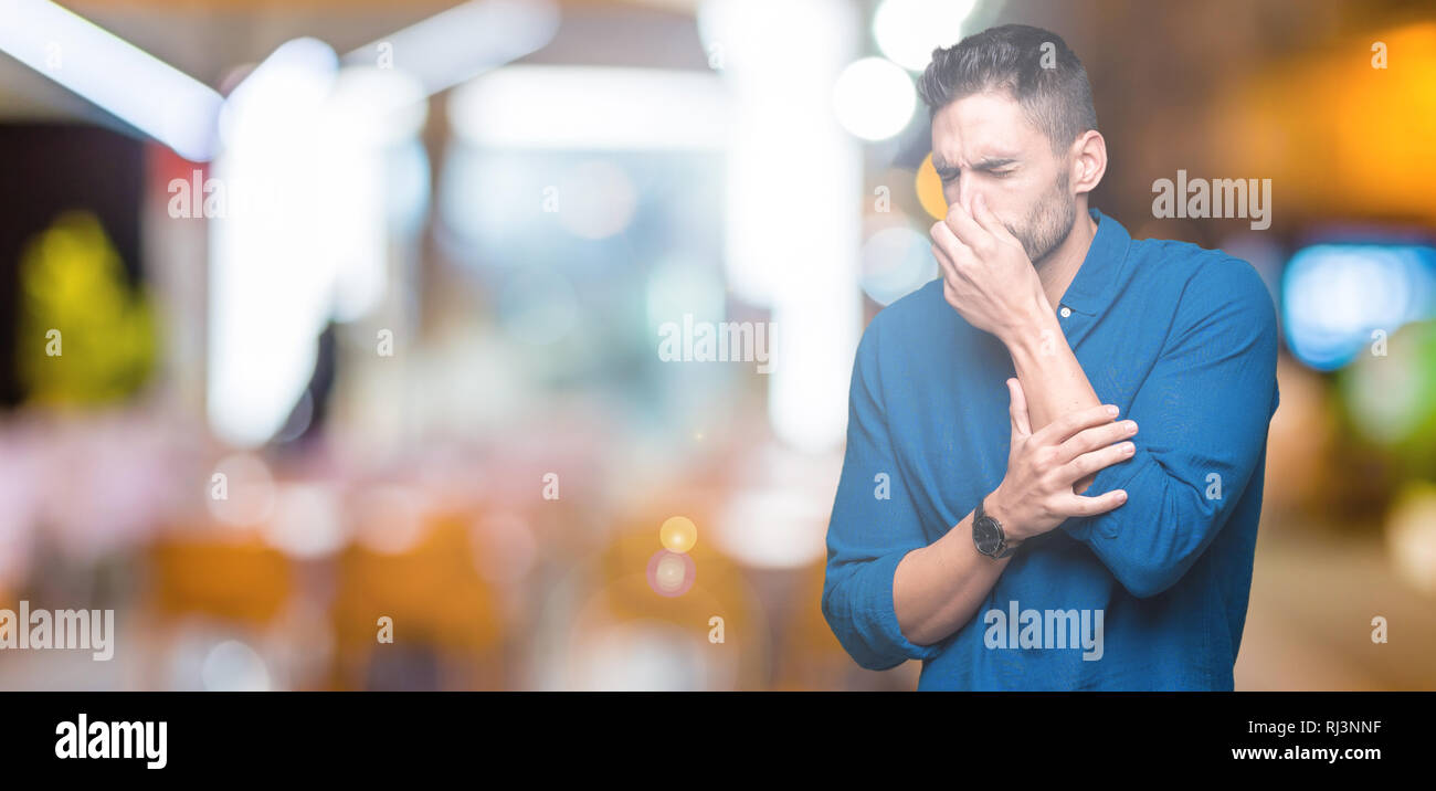 Young handsome man over isolated background smelling something stinky ...