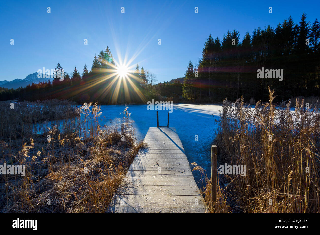 Wooden jetty with frozen lake and sun, Lake Geroldsee, Wagenbruechsee ...