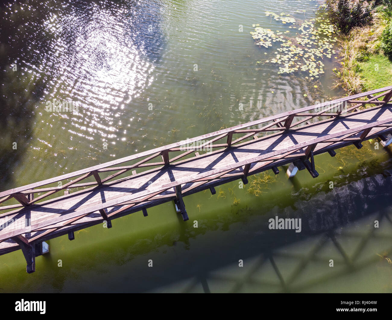 old wooden footbridge over river. sky and sun reflecting in greenish ...