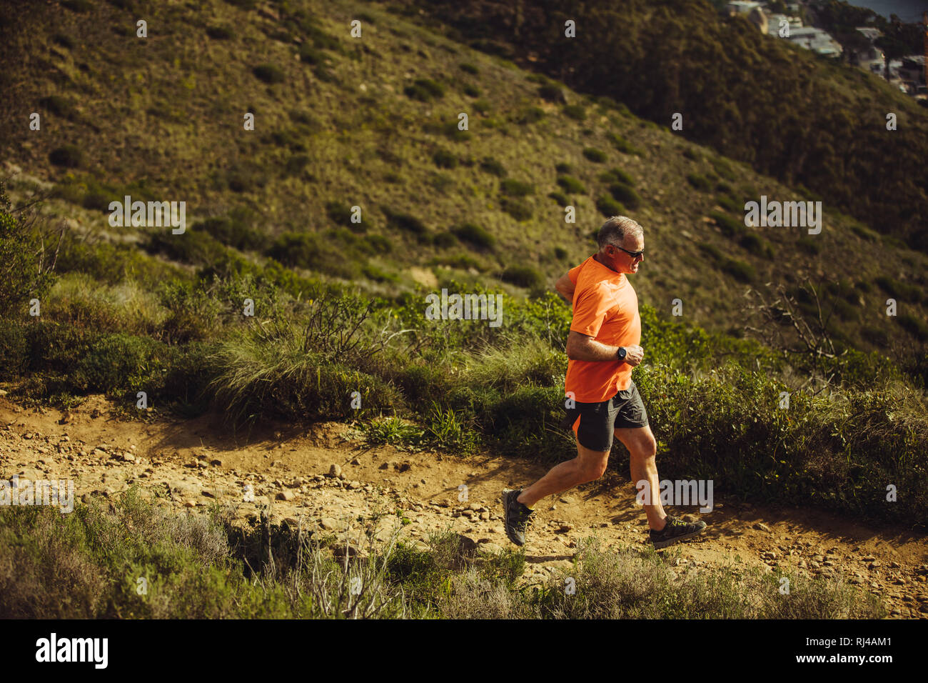 Athletic man trail running down a hill on a sunny day. High angle view ...