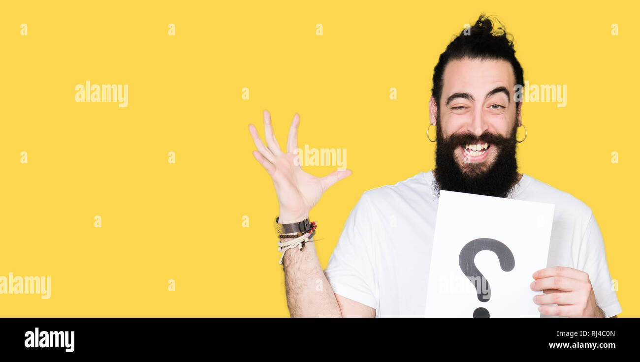 Young man with long hair and bear holding a paper with question mark ...