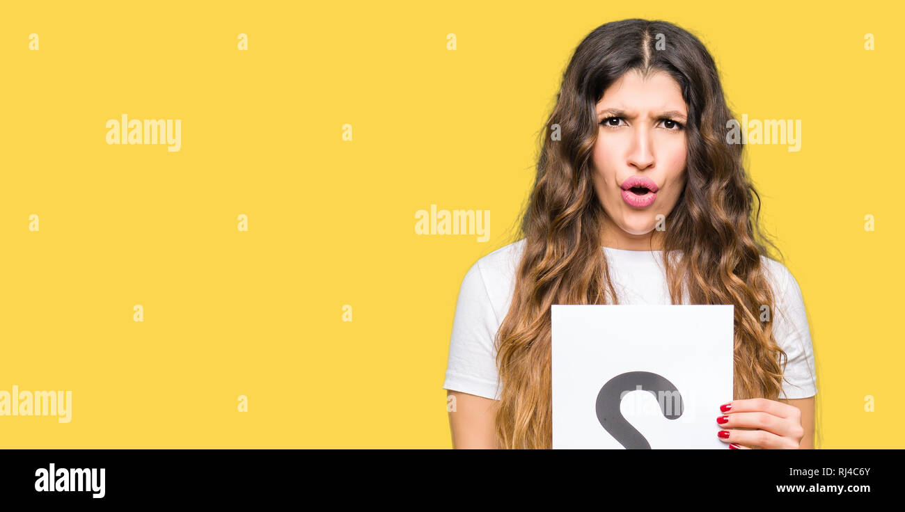 Young adult woman holding paper with question mark scared in shock with ...