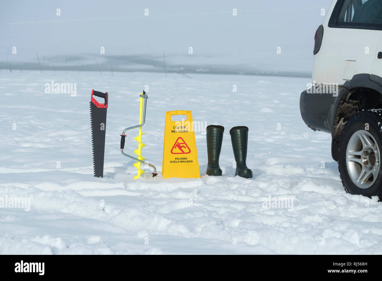 Saw, ice drill auger, signboard and boots on a snow. Selective focus ...