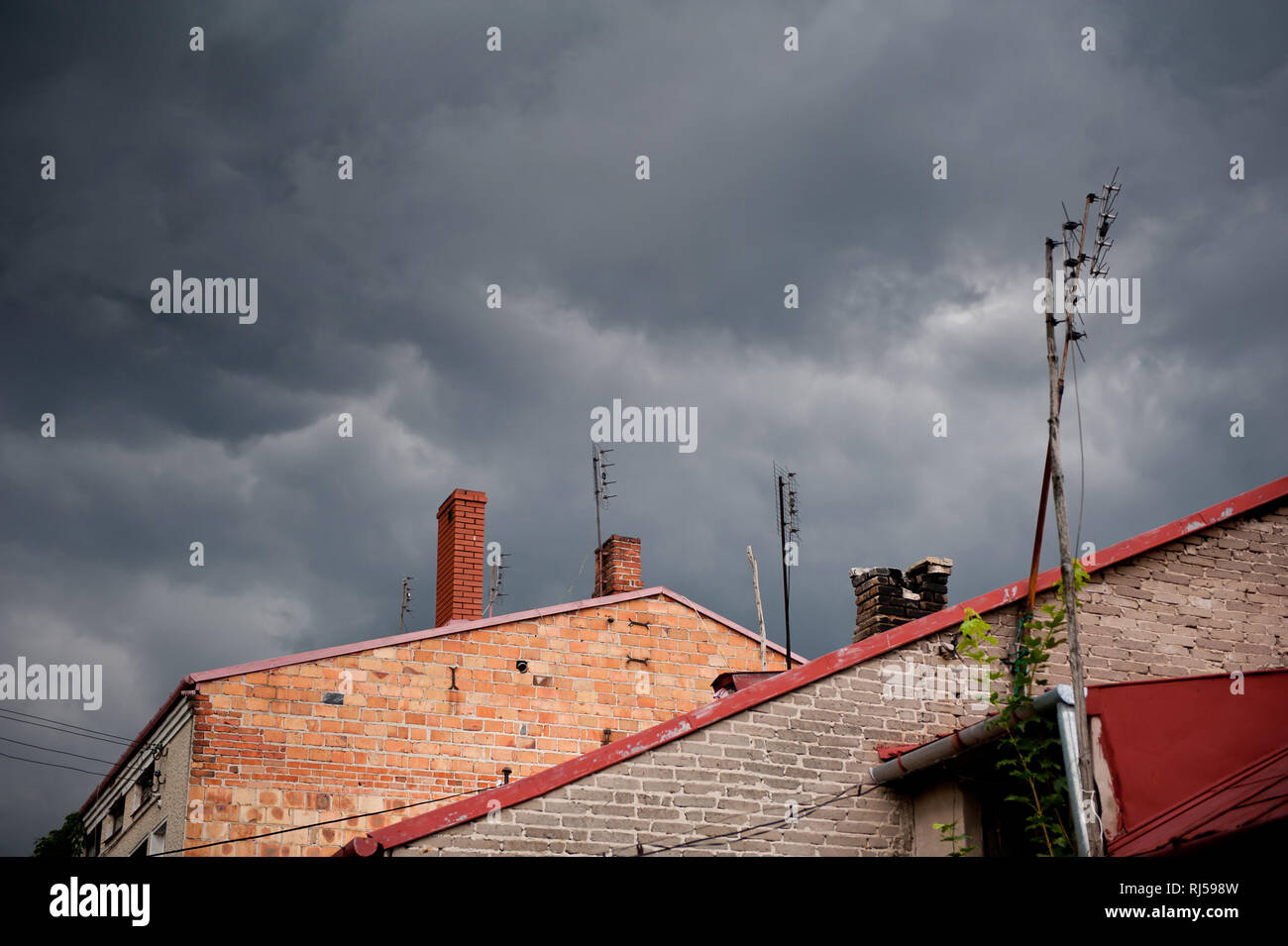 Gloomy clouds weather above brick houses with antenna and chimney on ...